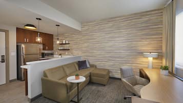 Quarto de hotel moderno com cozinha compacta, sofá, mesa redonda pequena e escrivaninha com luminária.
