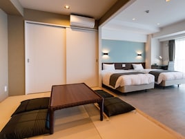 Quarto de hotel moderno com uma cama grande, um sofá-cama adicional, uma pequena mesa e um guarda-roupa com portas de correr.