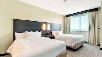 Quarto de hotel com duas camas, uma janela grande com cortinas e uma cabeceira moderna.