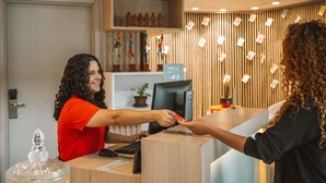 Bancada de recepção com computador, caixa registradora e uma estante decorativa com figuras.