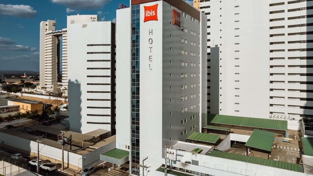 Um hotel moderno com um letreiro grande da 'ibis', rodeado por edifícios altos.