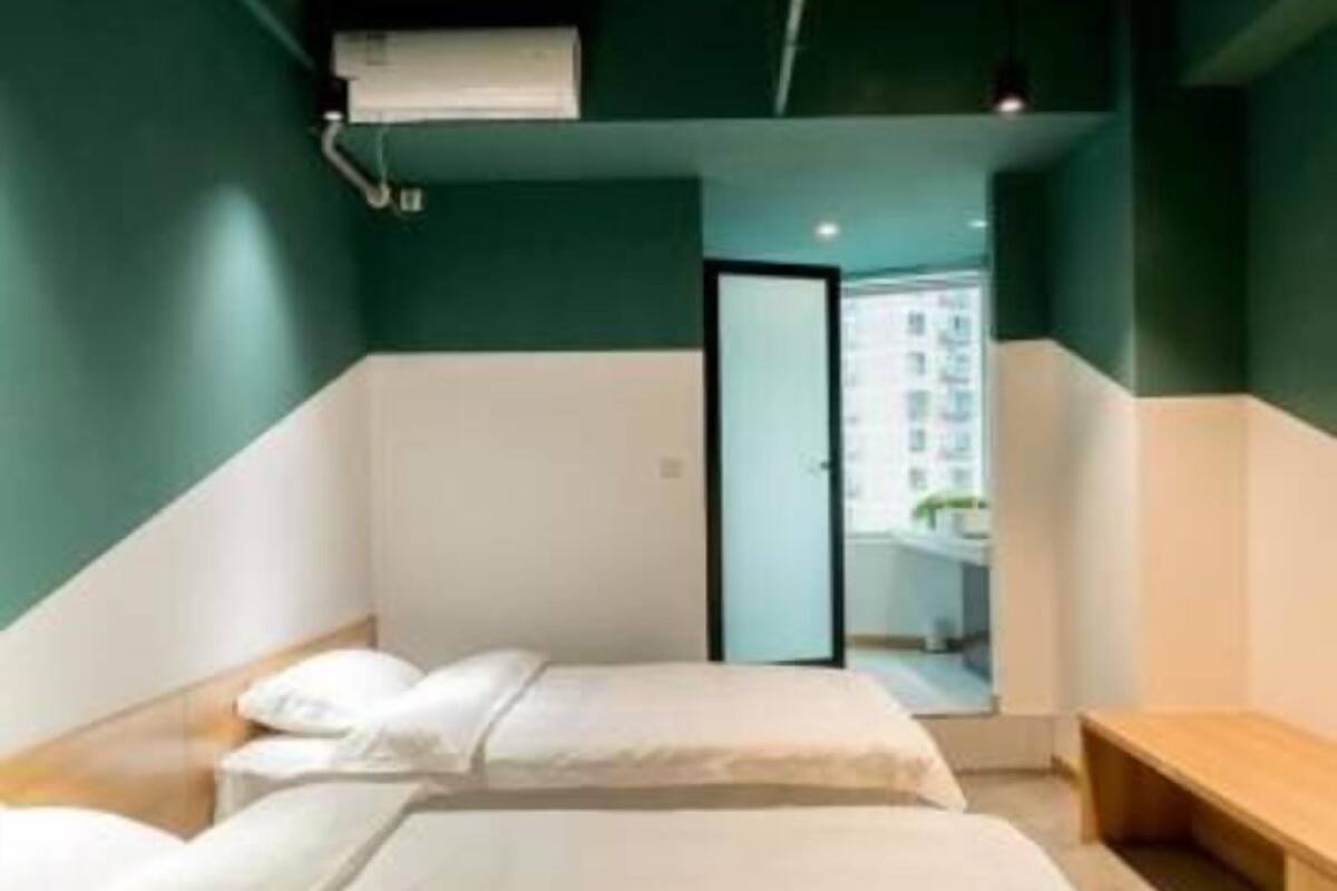 Quarto com duas camas, um banco de madeira e vista para um edifício através de uma porta de vidro.