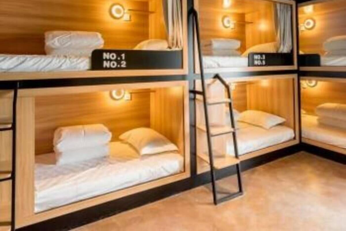 Quarto de hotel com beliches, cada um identificado com um número. Há uma escada para acessar o beliche superior.
