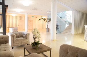 Um hall espaçoso com uma escadaria imponente, assentos confortáveis e um arranjo central de orquídeas em vaso.