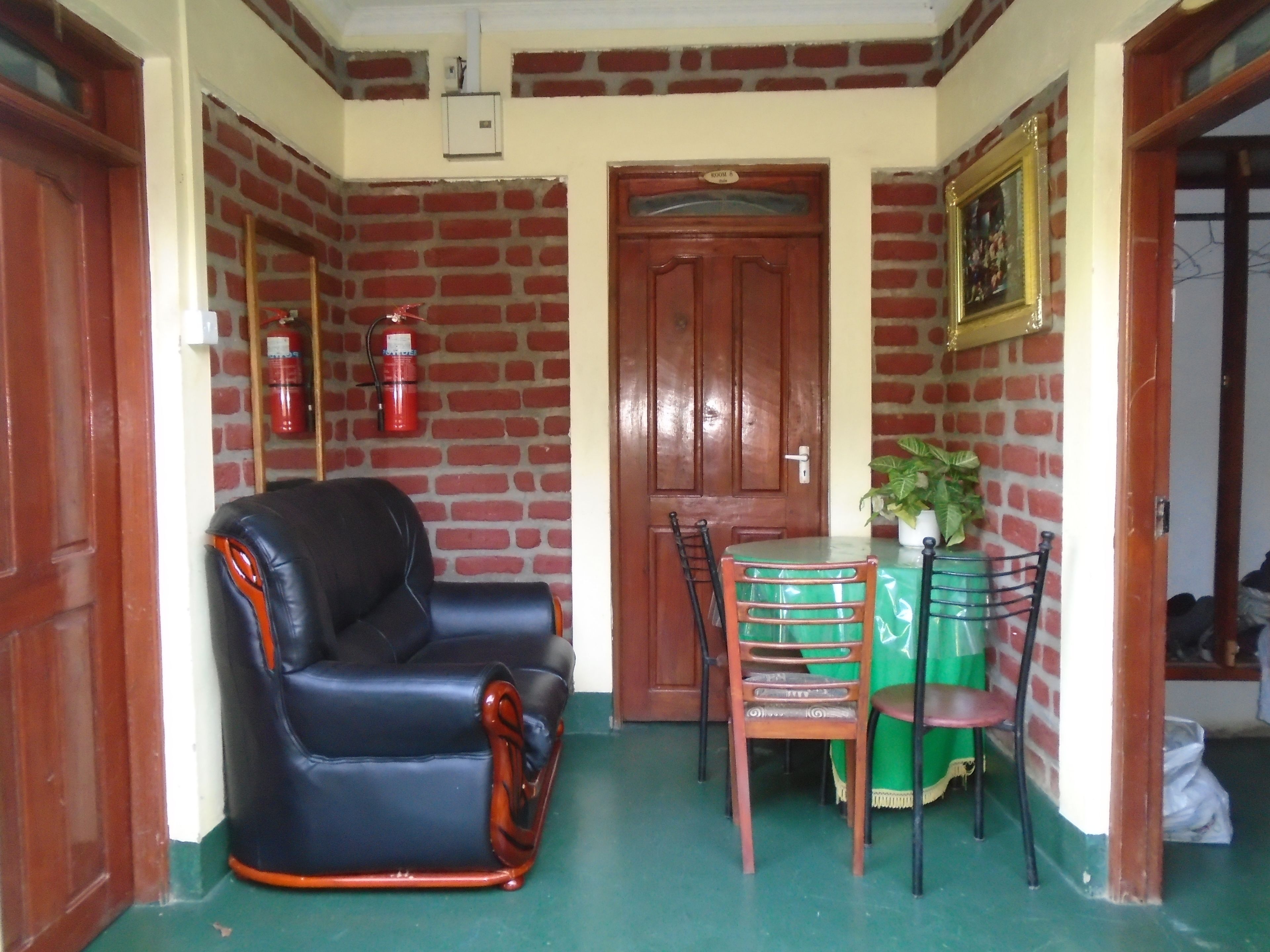 Um quarto com parede de tijolos, porta de madeira, sofá de couro preto, mesa de jantar de madeira com cadeiras e toalha de mesa verde.