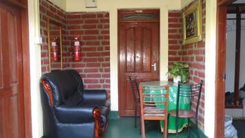 Um quarto com parede de tijolos, porta de madeira, sofá de couro preto, mesa de jantar de madeira com cadeiras e toalha de mesa verde.