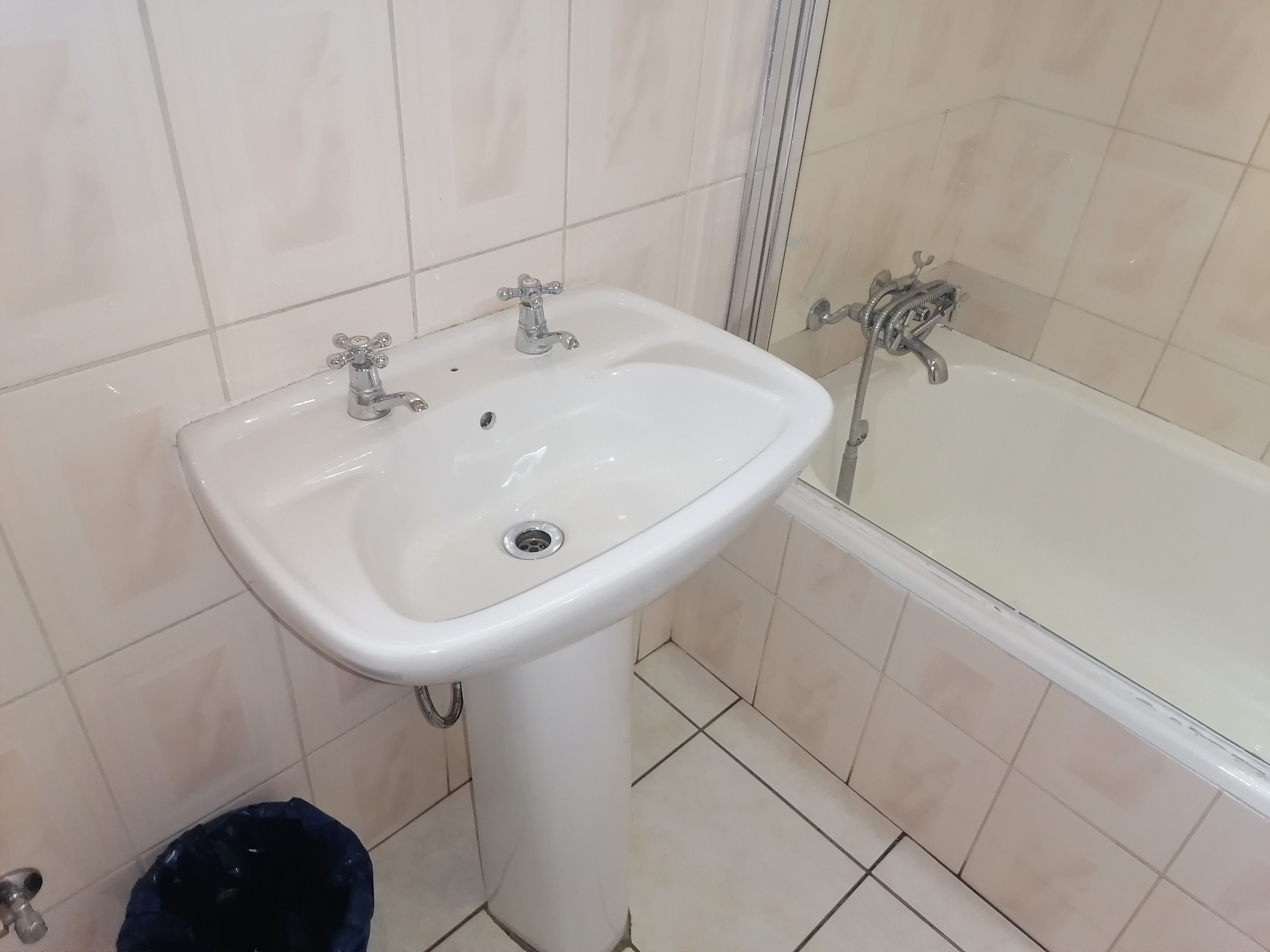 Casa de banho com lavatório pedestal branco, banheira e um cesto de lixo azul.