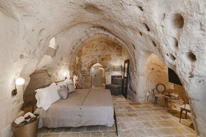 Quarto com arco de pedra, uma cama, uma cadeira, uma mesa e um espelho.