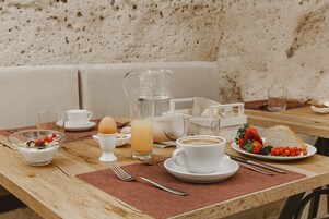 Mesa de café da manhã posta com um jarro, xícaras, um prato de frutas e um copo de suco de laranja.