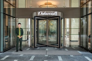 Uma porta giratória com a placa "Oakwood" acima, uma pessoa em frente e fachada de um edifício moderno com janelas de vidro.
