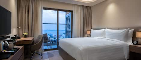 Quarto de hotel moderno com uma cama grande, uma escrivaninha com computador, uma cadeira e uma televisão.