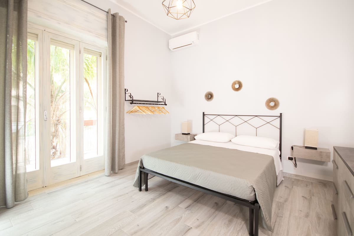 Quarto com cama, mesas de cabeceira, luminária pendente e vista para o exterior.