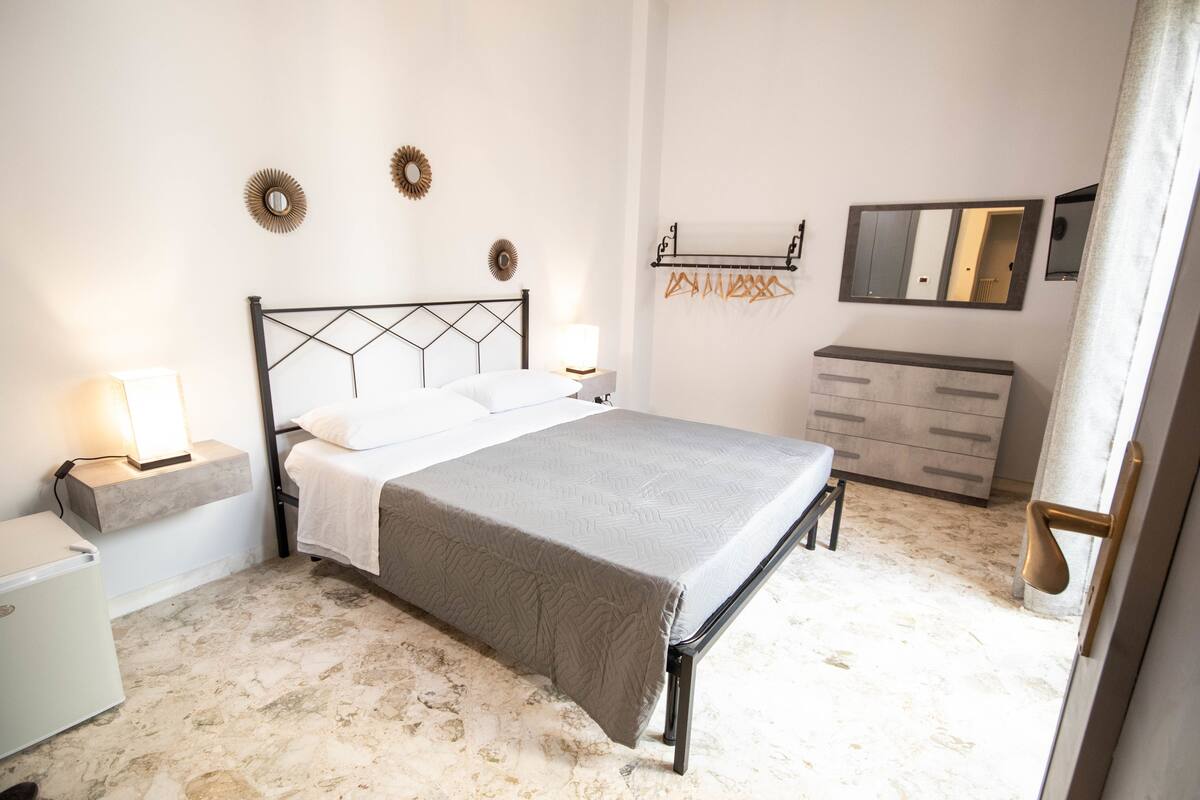 Quarto com cama, mesas de cabeceira, cômoda e espelho.