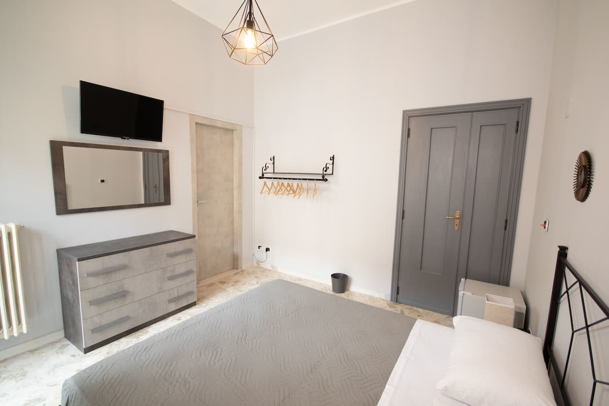 Um quarto com uma cama, cômoda, televisão, porta e um cabideiro.