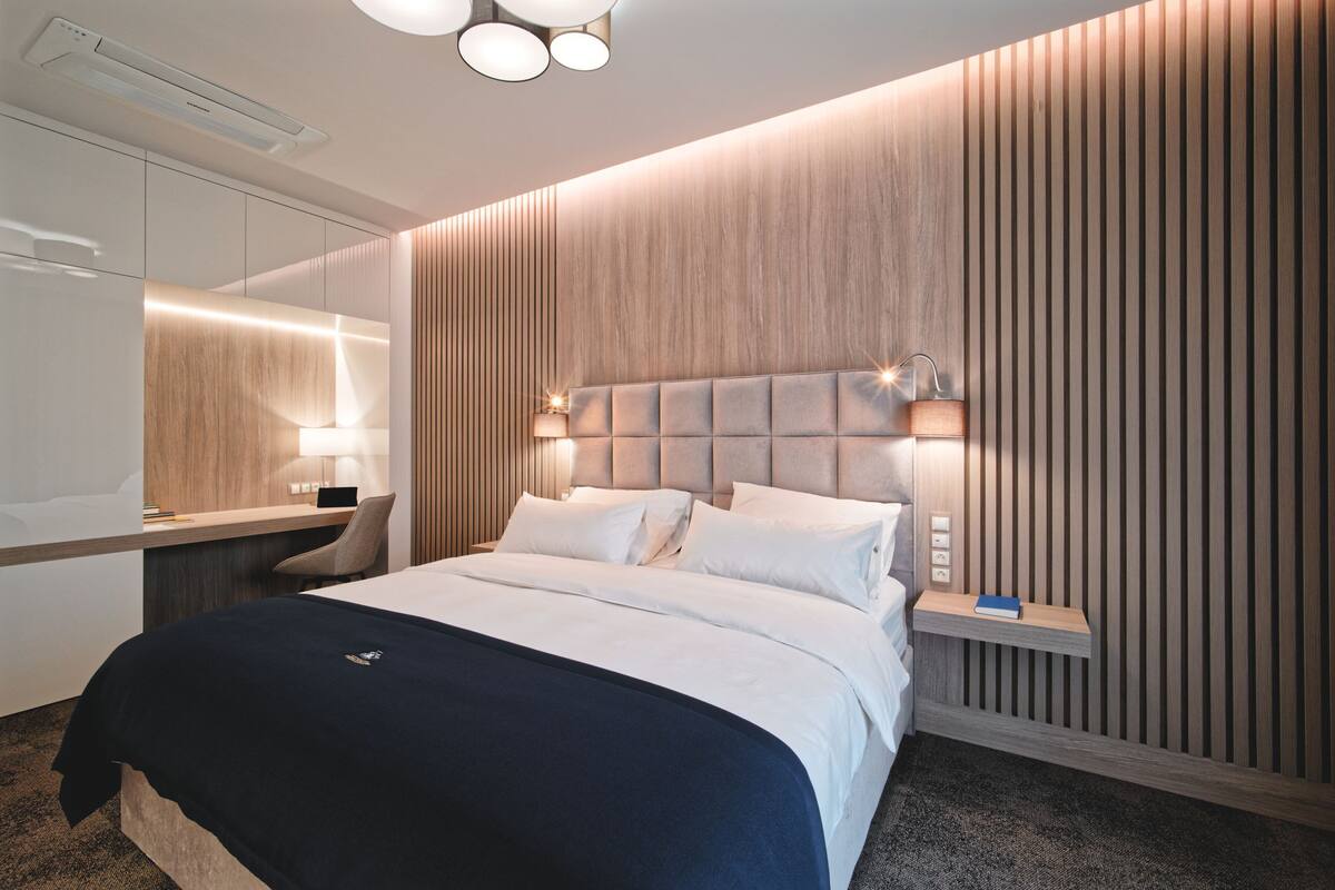 Quarto de hotel moderno com uma cama grande, mesas de cabeceira, uma escrivaninha e um espelho.