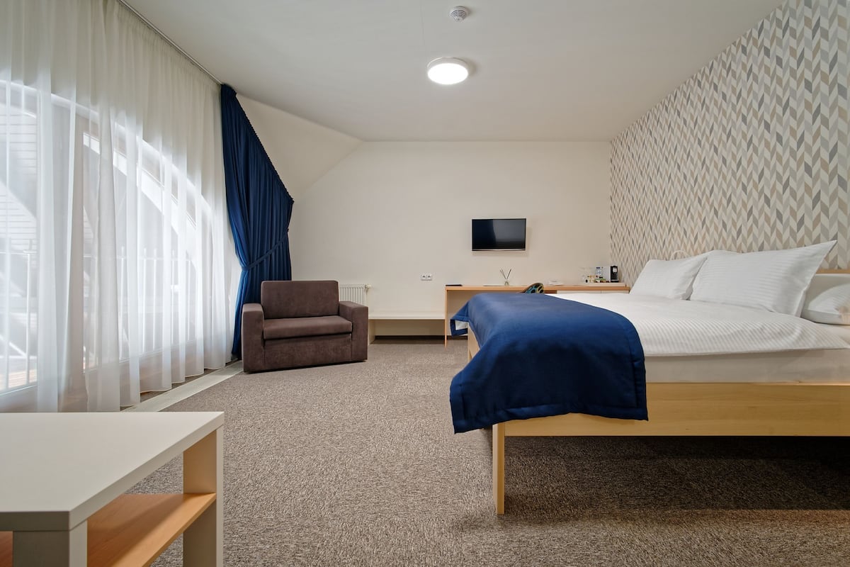 Quarto de hotel com cama, escrivaninha, cadeira e televisão na parede.