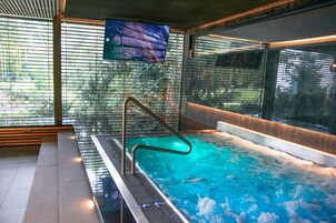 Uma piscina interior moderna com barreira de vidro, uma televisão na parede e vista para o exterior através de grandes janelas.