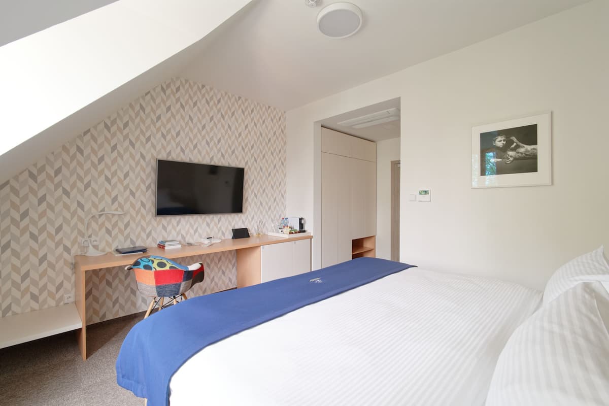 Quarto com cama, escrivaninha com cadeira, televisão e porta que dá para outro espaço.