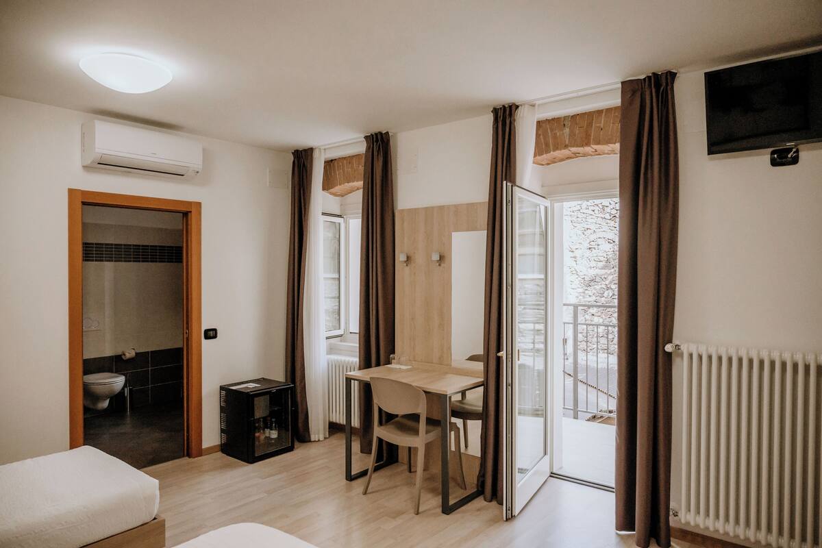 Quarto com mesa de madeira, uma cadeira, uma cama, radiador e televisão na parede.