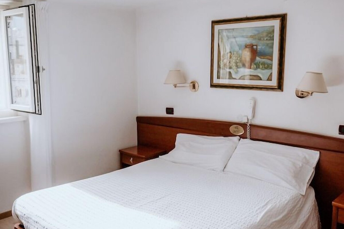 Cama bem arrumada com cabeceira de madeira, duas luminárias de apoio e um quadro na parede.