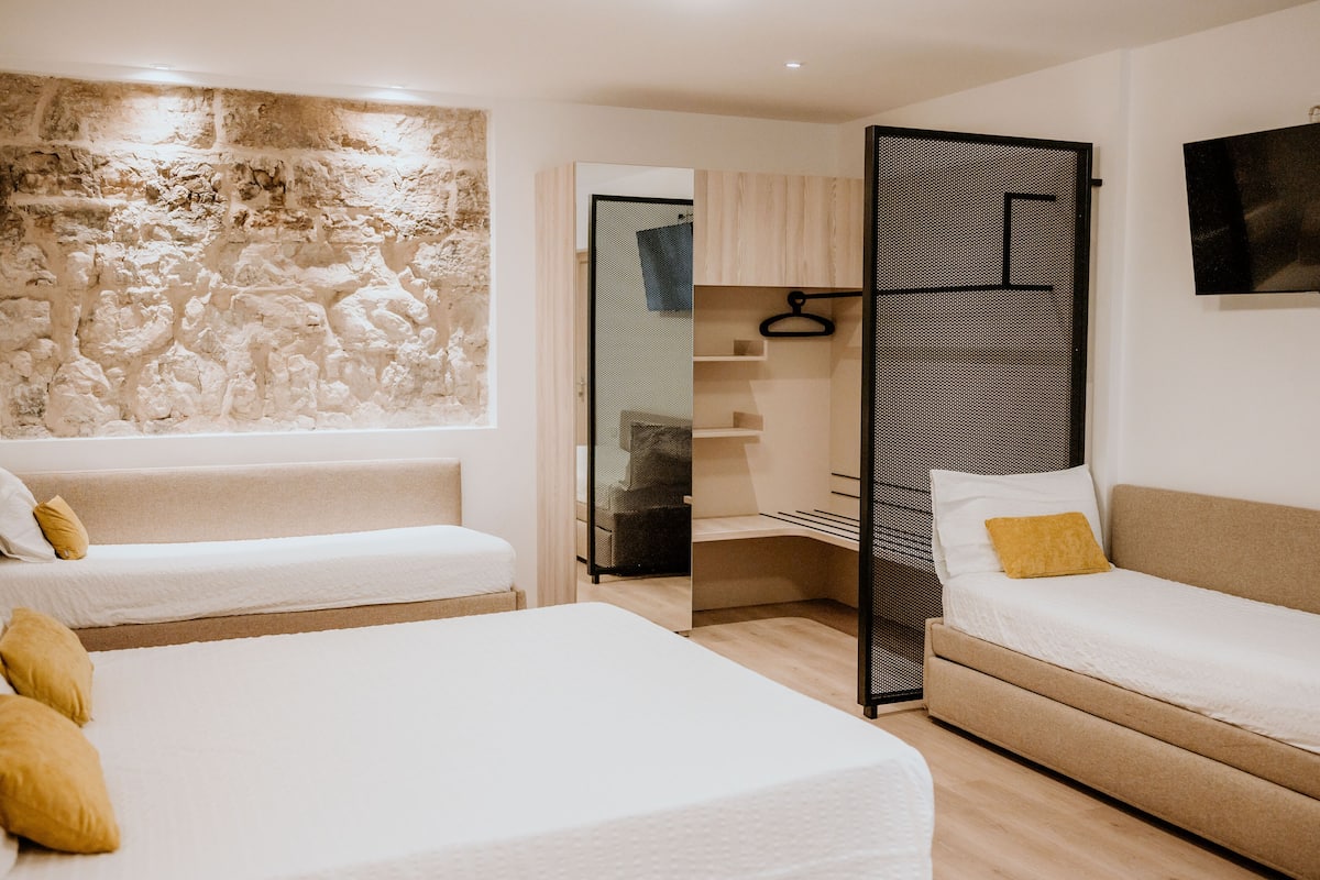 Quarto de hotel moderno com duas camas, parede de pedra, armário de madeira e divisória preta.
