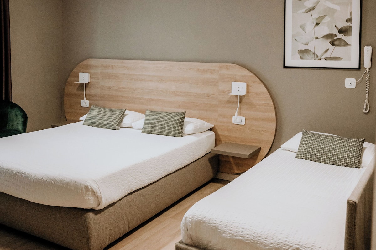 Quarto de hotel com duas camas, uma cabeceira de madeira, luminárias de cabeceira, um telefone e uma obra de arte emoldurada na parede.