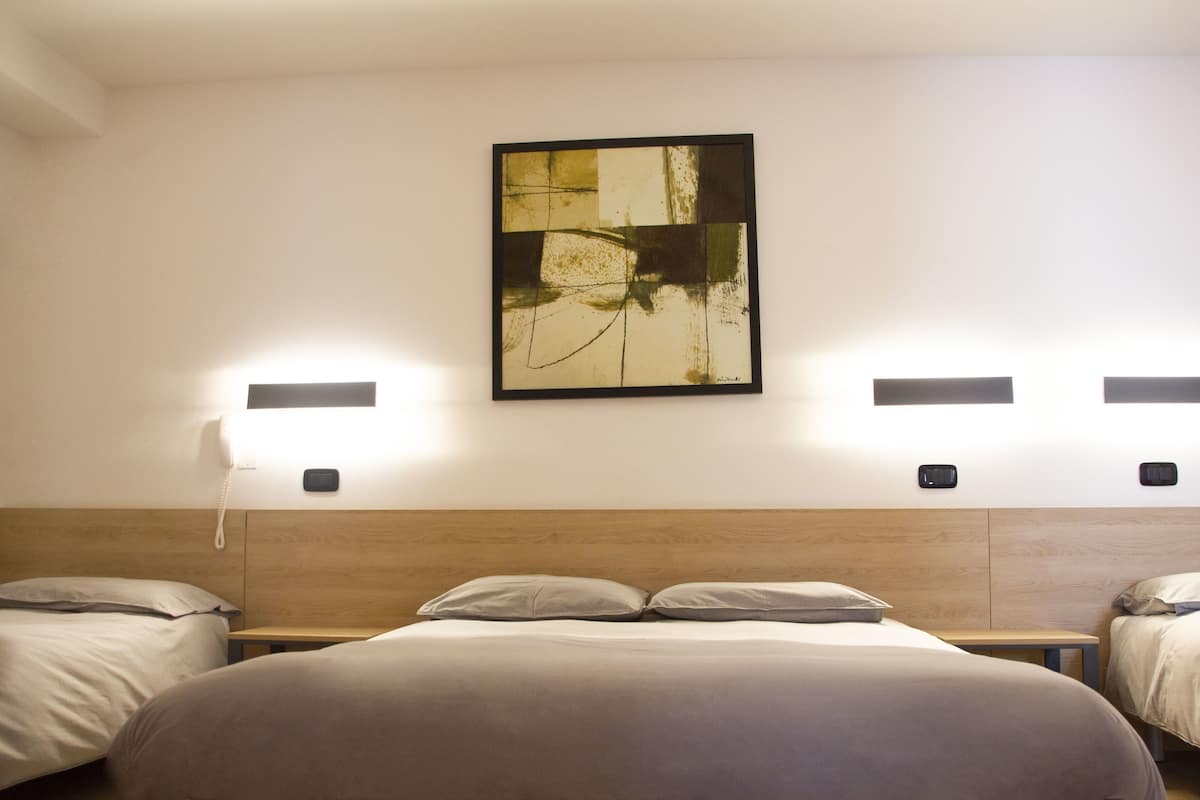 Quarto de hotel com uma cama grande, duas mesas de cabeceira, um quadro abstrato pendurado na parede e duas luminárias fixadas na parede.