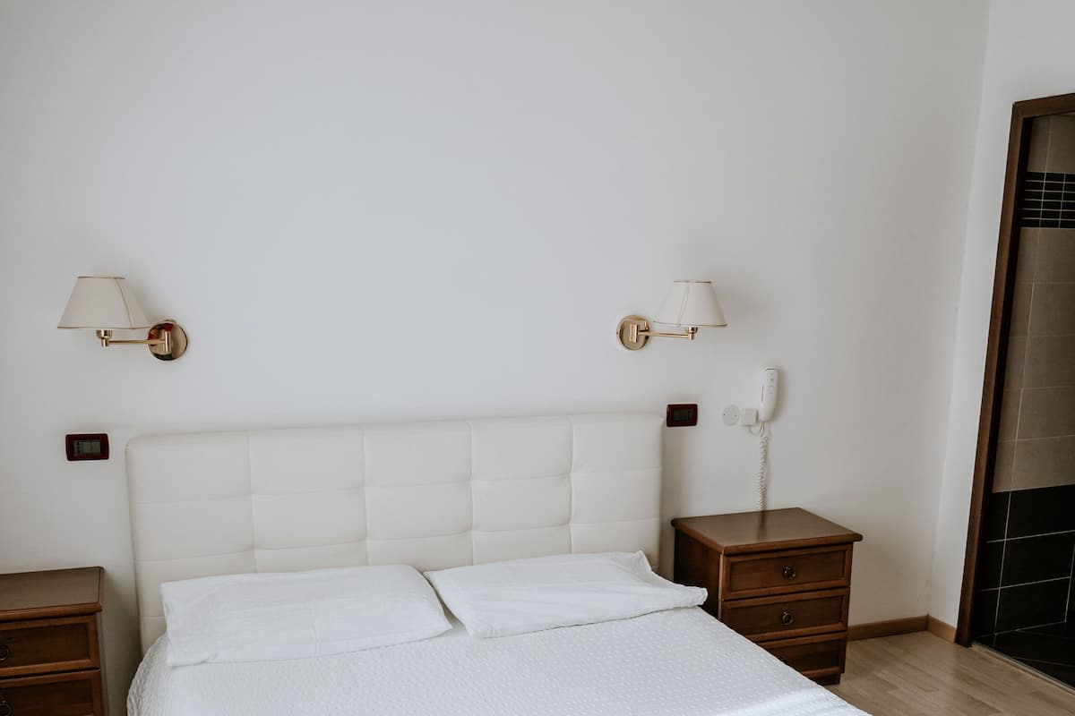 Um quarto bem arrumado com uma cama grande, mesas de cabeceira e um telefone fixado na parede.