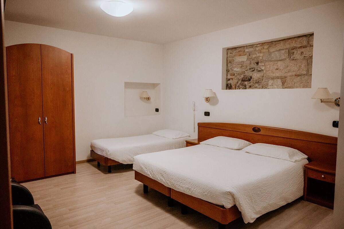 Quarto de hotel com duas camas de solteiro, um guarda-roupa de madeira, um ornamento de parede de pedra e uma pequena luminária na parede.