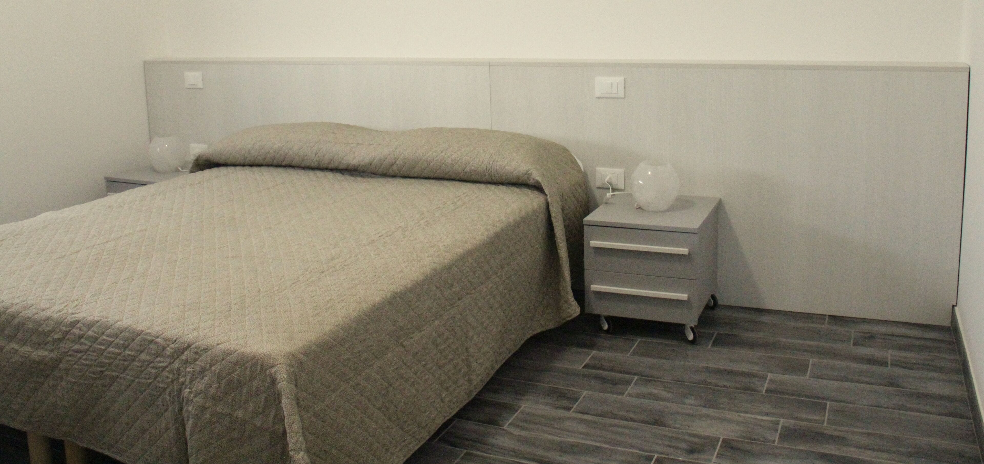 Um quarto com cama, mesa de cabeceira e criado-mudo.