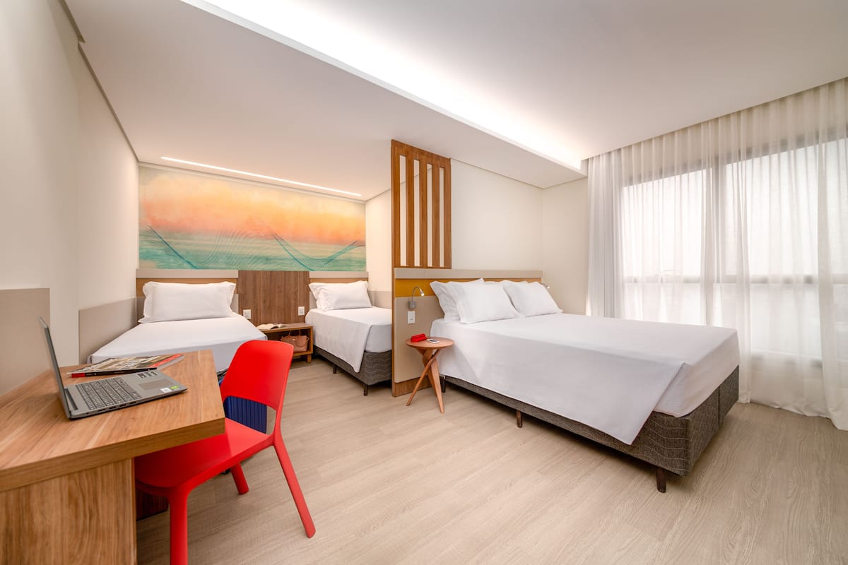 Quarto de hotel com duas camas, uma escrivaninha, uma cadeira e um quadro na parede.