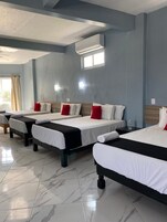 Quarto de hotel com quatro camas dispostas em linha, piso de ladrilho de mármore e um aparelho de ar condicionado na parede.