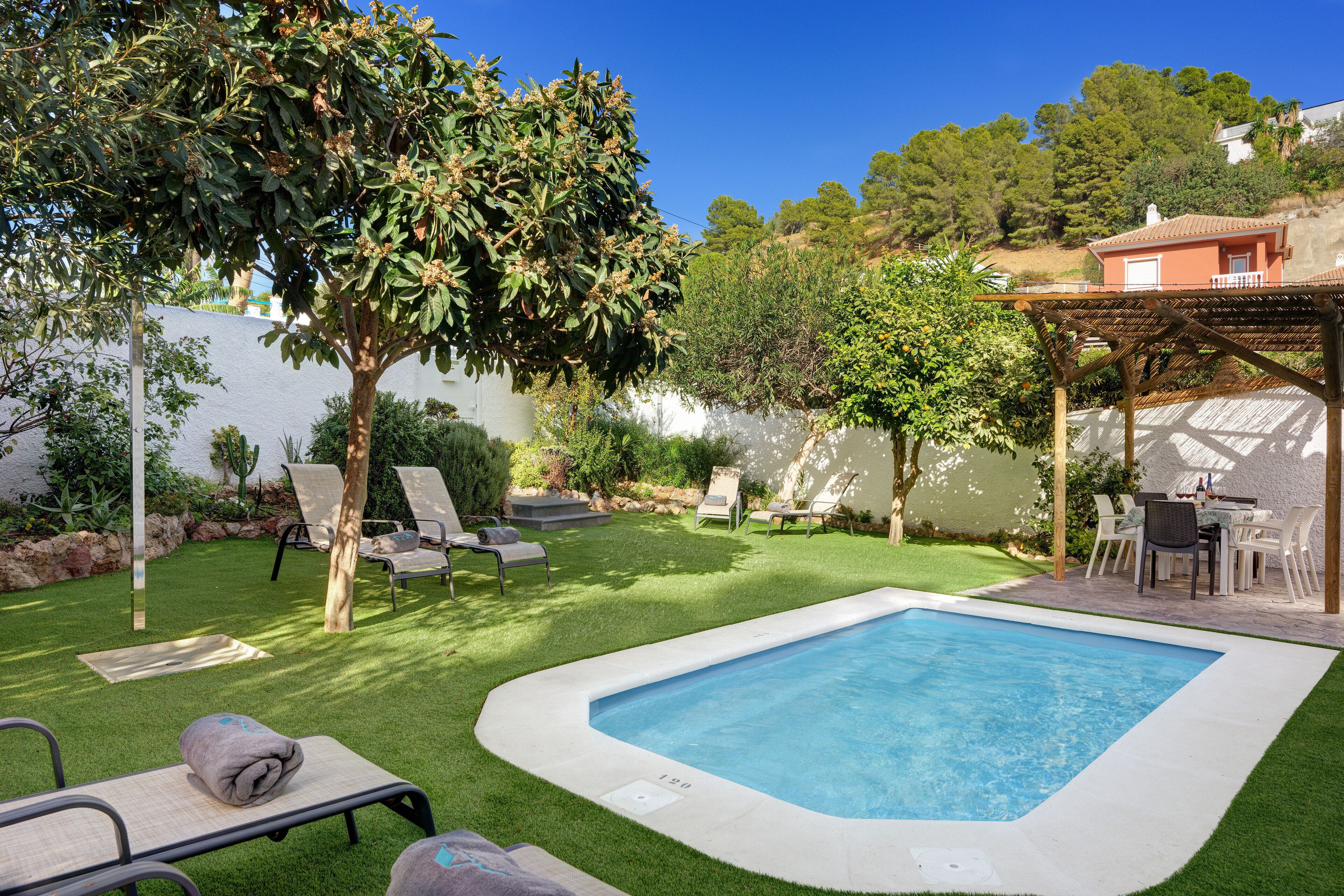 Um quintal com piscina, cadeiras de sol, pérgola e área de refeições.
