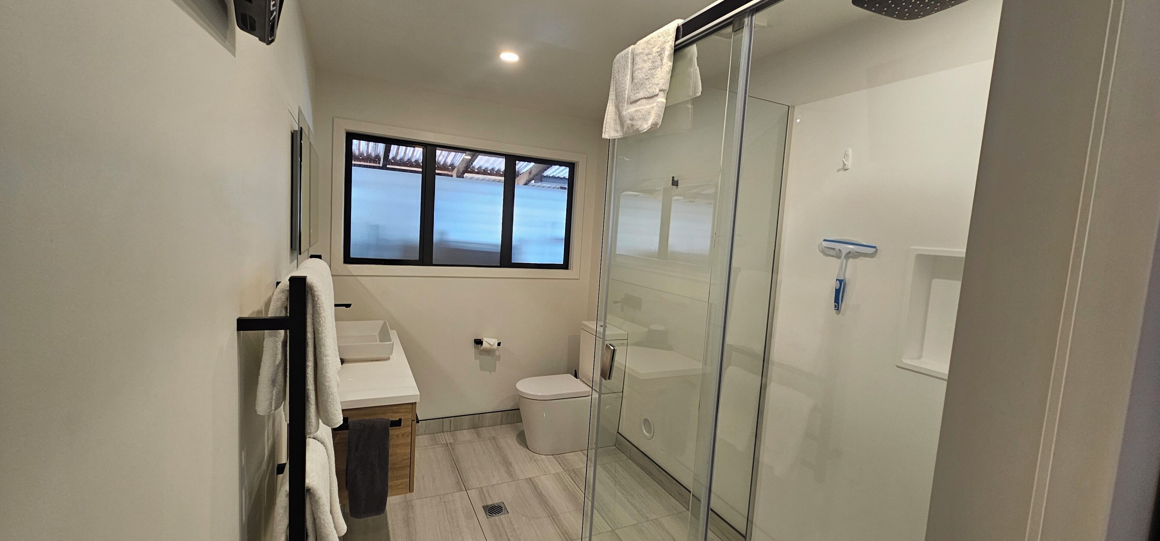 Uma casa de banho moderna com cabine de chuveiro em vidro, sanita, lavatório e janela com vidro jateado.