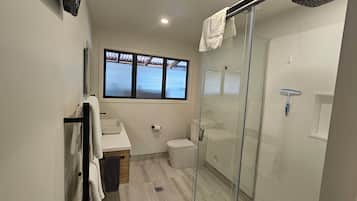 Uma casa de banho moderna com cabine de chuveiro em vidro, sanita, lavatório e janela com vidro jateado.
