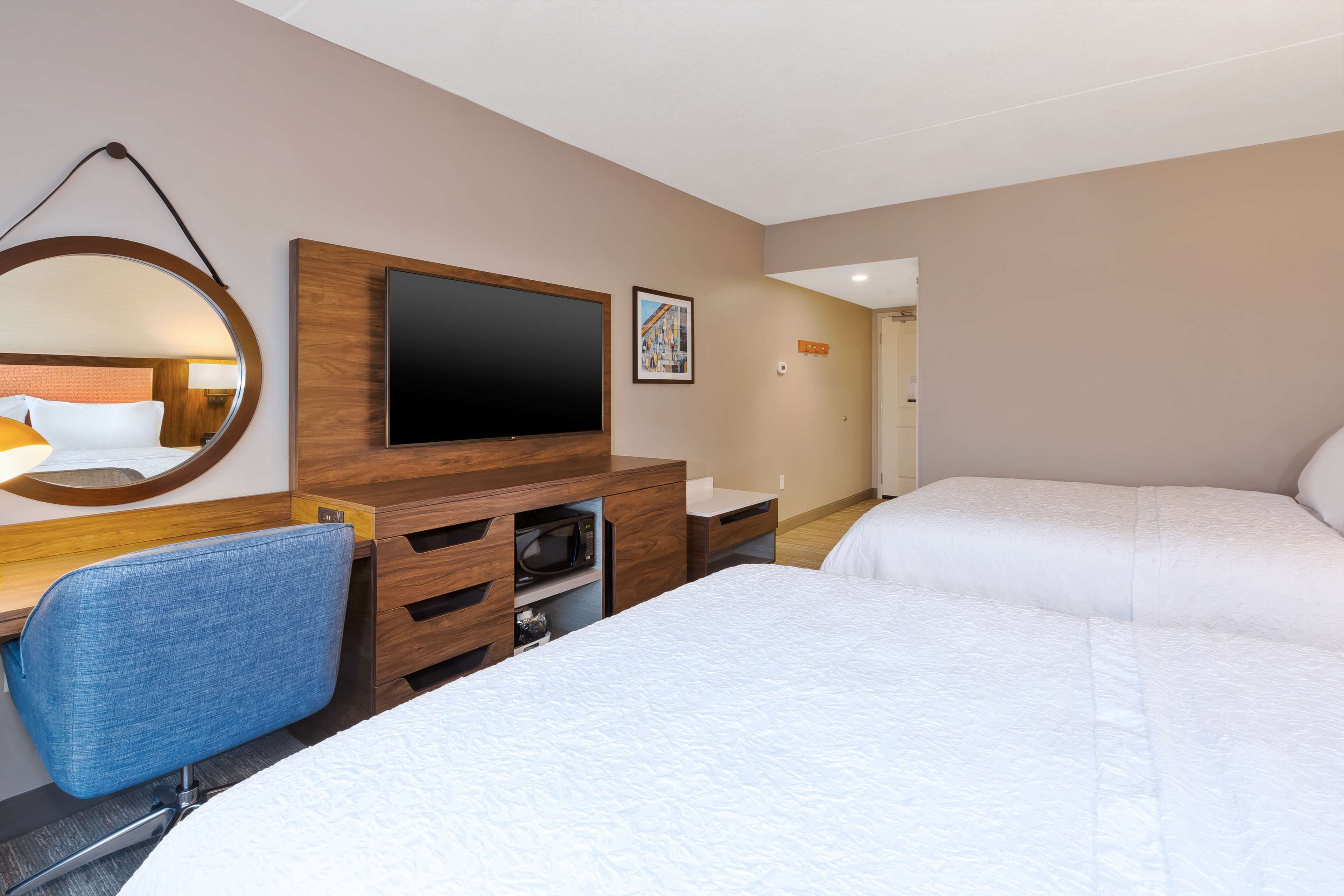 Quarto de hotel com duas camas, uma escrivaninha com cadeira, uma televisão e um espelho.