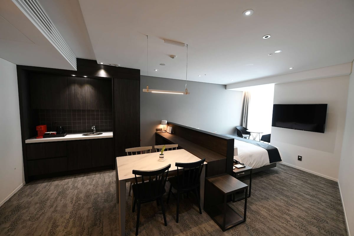 Quarto de hotel compacto com cozinha compacta, área de refeições, cama e televisão na parede.