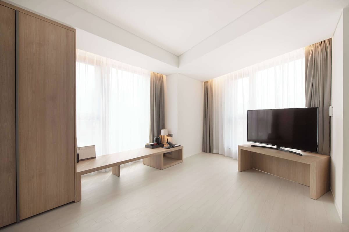 Quarto de hotel moderno com uma televisão de tela plana grande, um banco de madeira e uma escrivaninha com abajur.