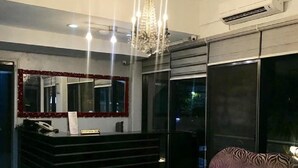 Uma área de recepção com um balcão moderno, um candelabro, um sofá e janelas amplas.