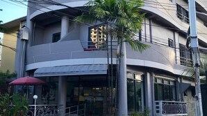 Um hotel moderno com fachada curva, várias varandas e uma entrada destacada com um guarda-sol vermelho.