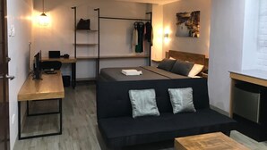 Quarto compacto com cama, escrivaninha, armário e pequena cozinha.