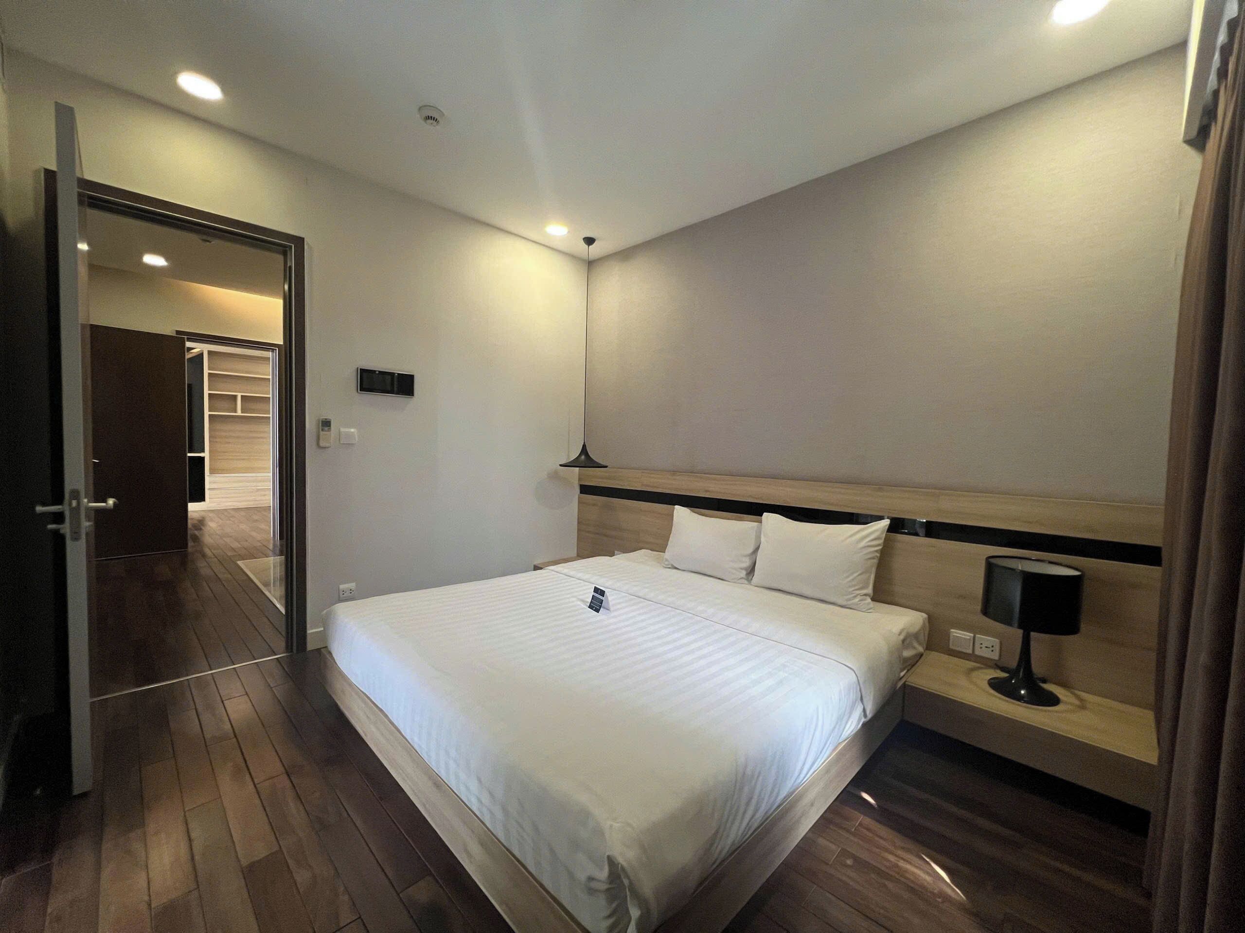 Quarto de hotel com uma cama grande, mesa de cabeceira com abajur, guarda-roupa e porta que dá para outro cômodo.