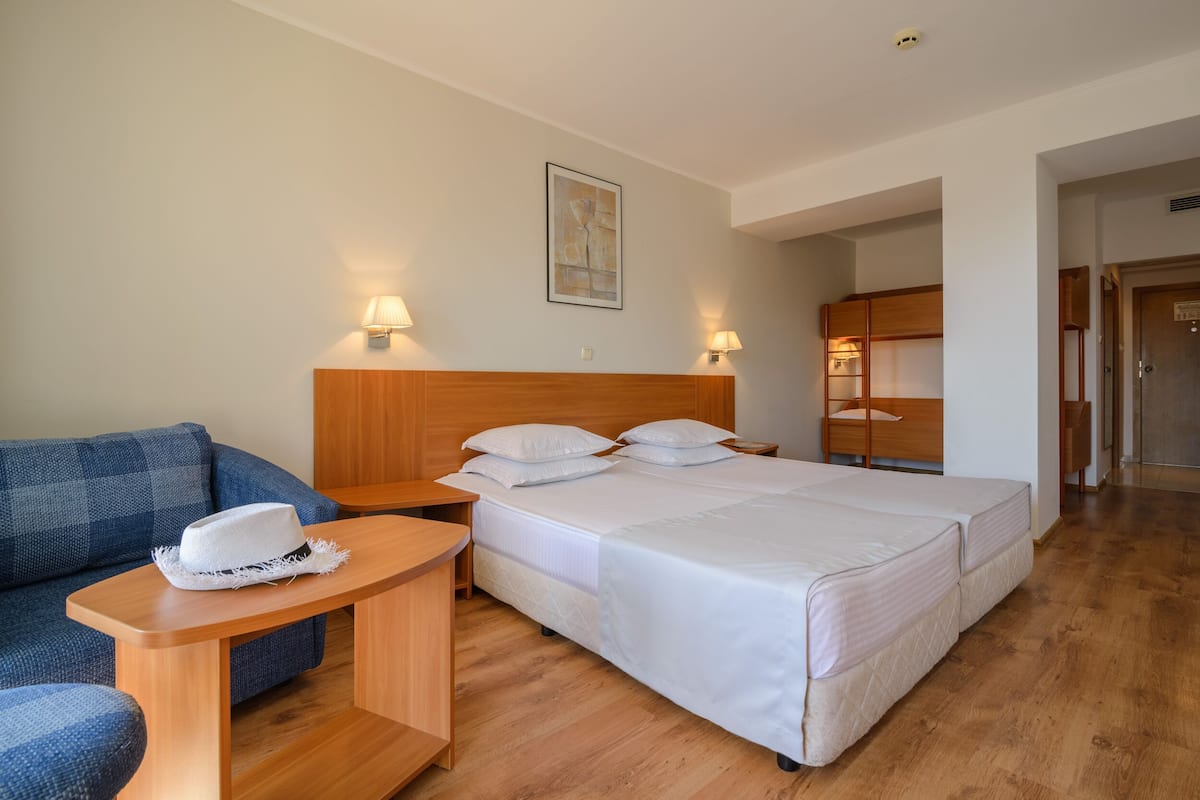 Quarto de hotel com cama, sofá, mesa pequena e mesa de cabeceira.