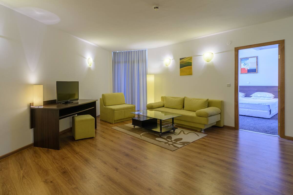 Uma sala de estar moderna com piso de madeira, um sofá, uma mesa de centro, uma televisão e uma escrivaninha.