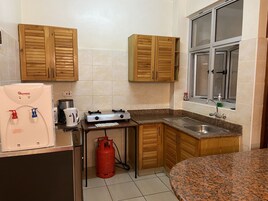Uma cozinha compacta com armários de madeira, fogão a gás, dispenser de água e pia.