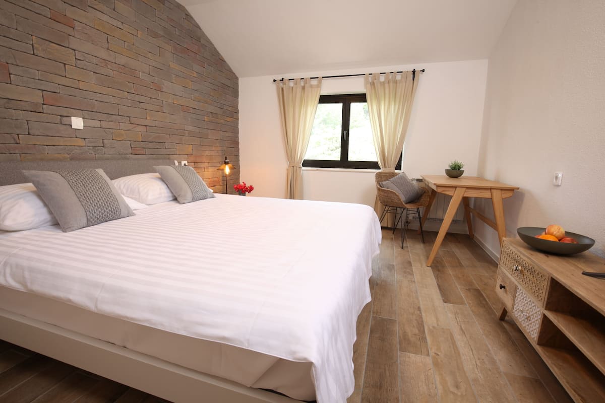 Quarto com uma cama grande, escrivaninha de madeira, uma cadeira e uma pequena mesa com uma tigela de frutas.