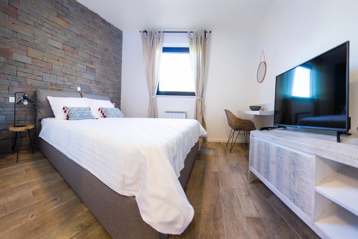 Quarto com cama, televisão, cadeira e parede de pedra.