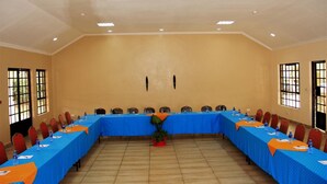 Sala de conferência com uma mesa comprida, cadeiras e toalha de mesa azul.