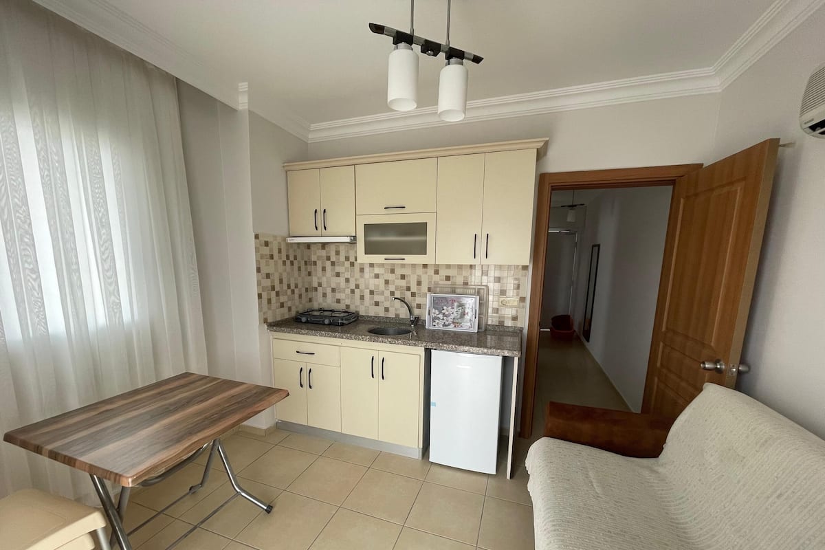 Cozinha compacta com micro-ondas, fogão e pia, uma mesa de jantar com cadeiras e um sofá.