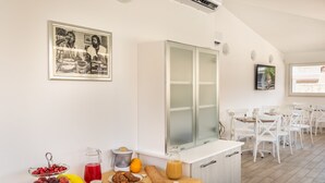 Disposição para o café da manhã com frutas, doces e bebidas sobre uma mesa, um armário e uma televisão ao fundo.